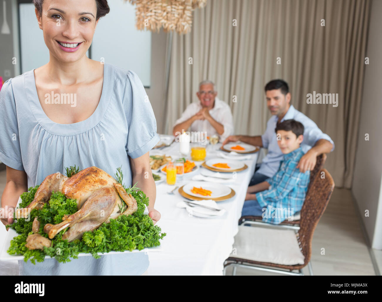 Portrait of a woman holding chicken roast with family at dining table ...
