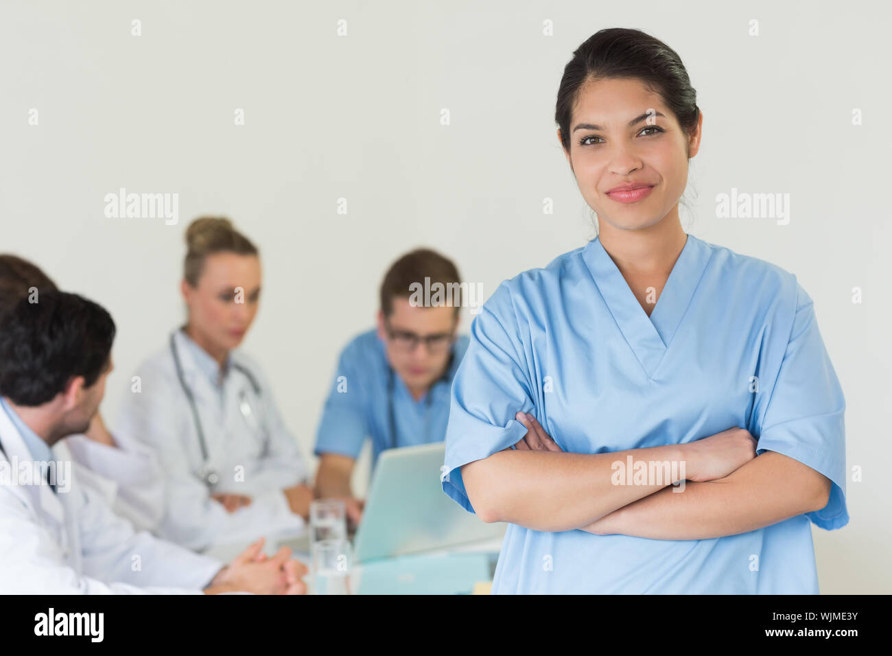 Portrait of female nurse standing arms crossed with colleagues in ...