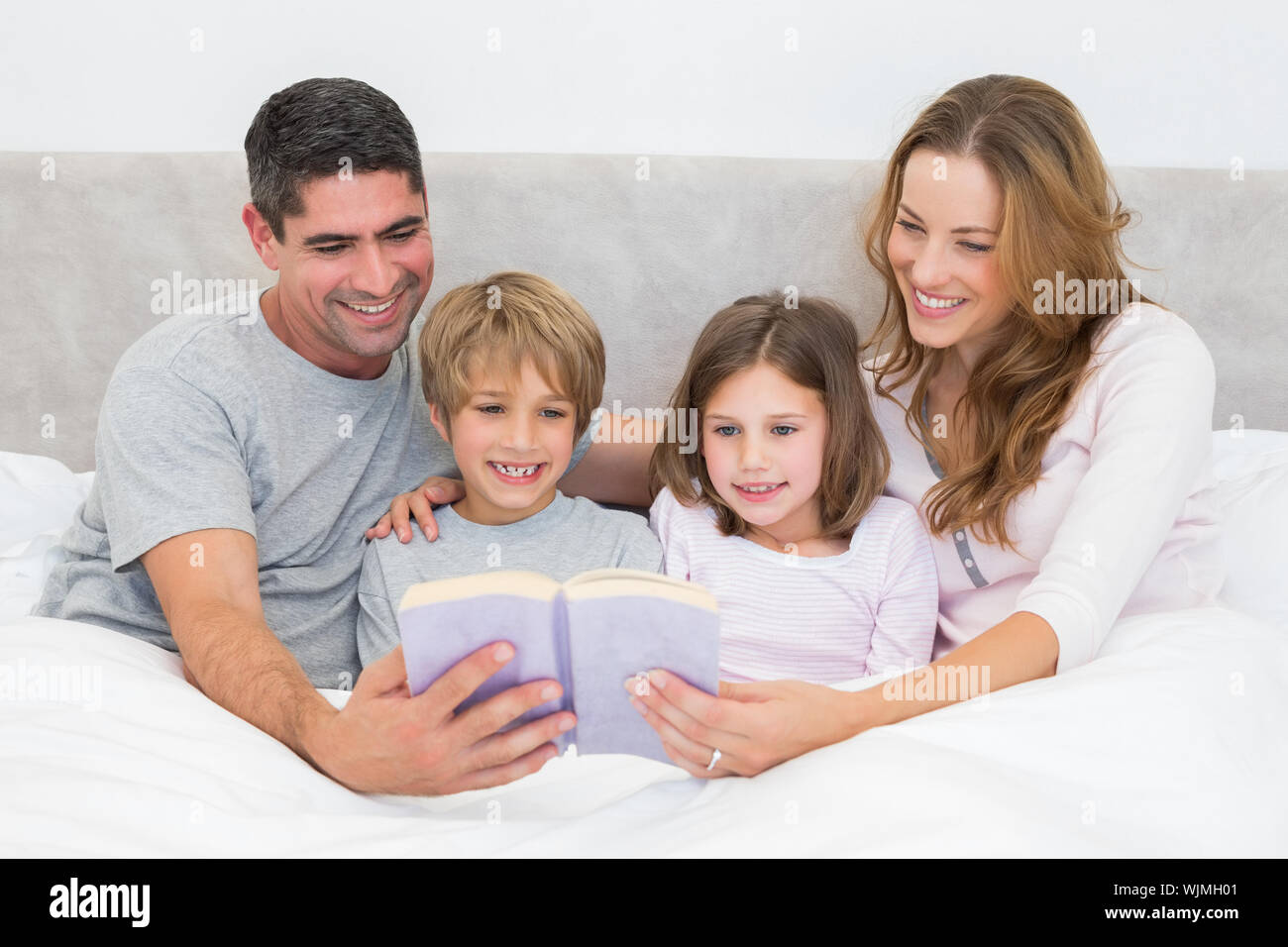 Smiling family reading storybook in bed Stock Photo - Alamy