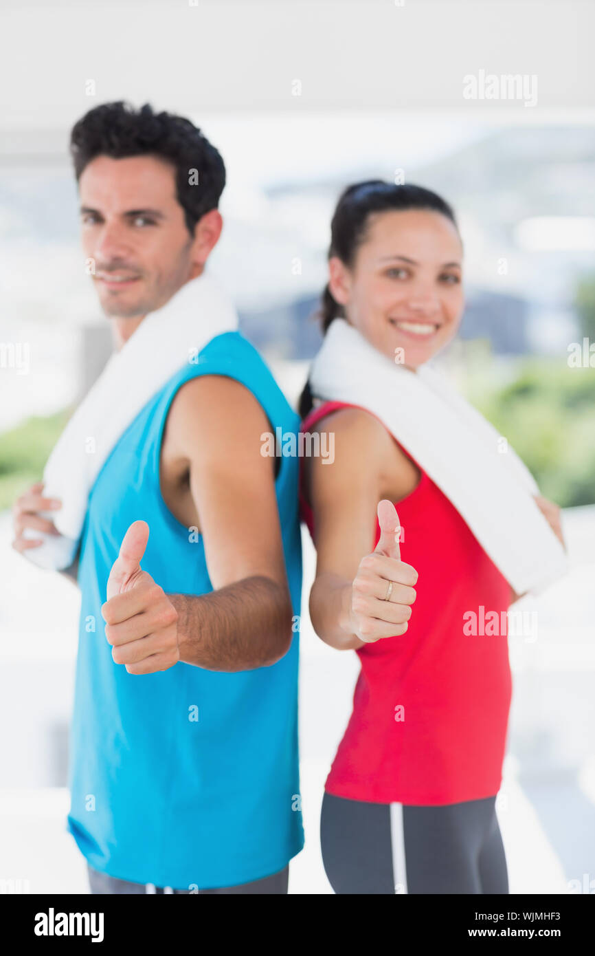 Portrait of a fit young couple gesturing thumbs up in a bright exercise ...