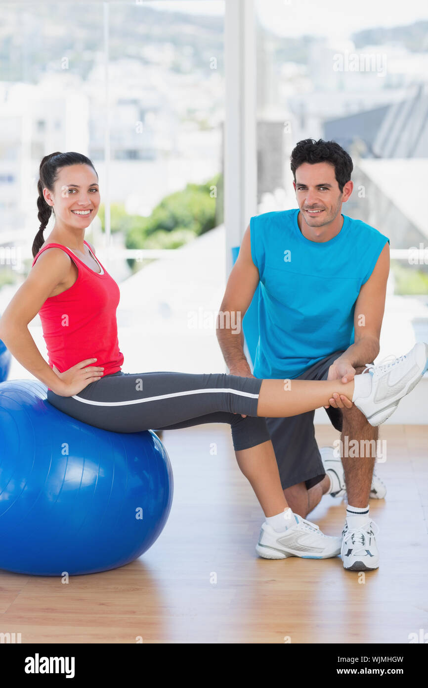 Smiling male trainer helping woman with her exercises at a bright gym ...