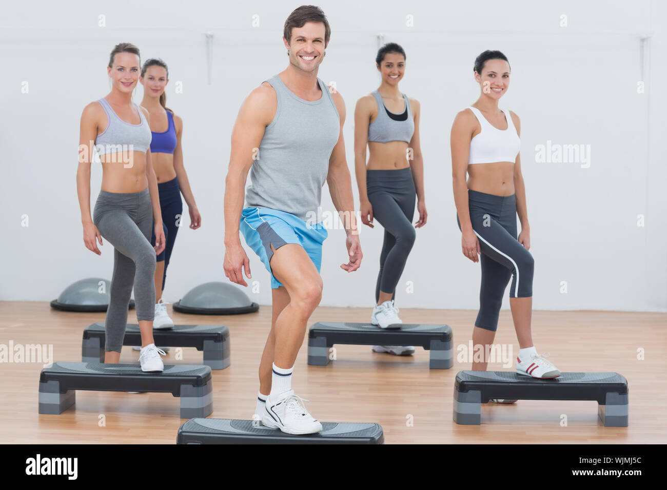 Full length of instructor with fitness class performing step aerobics ...