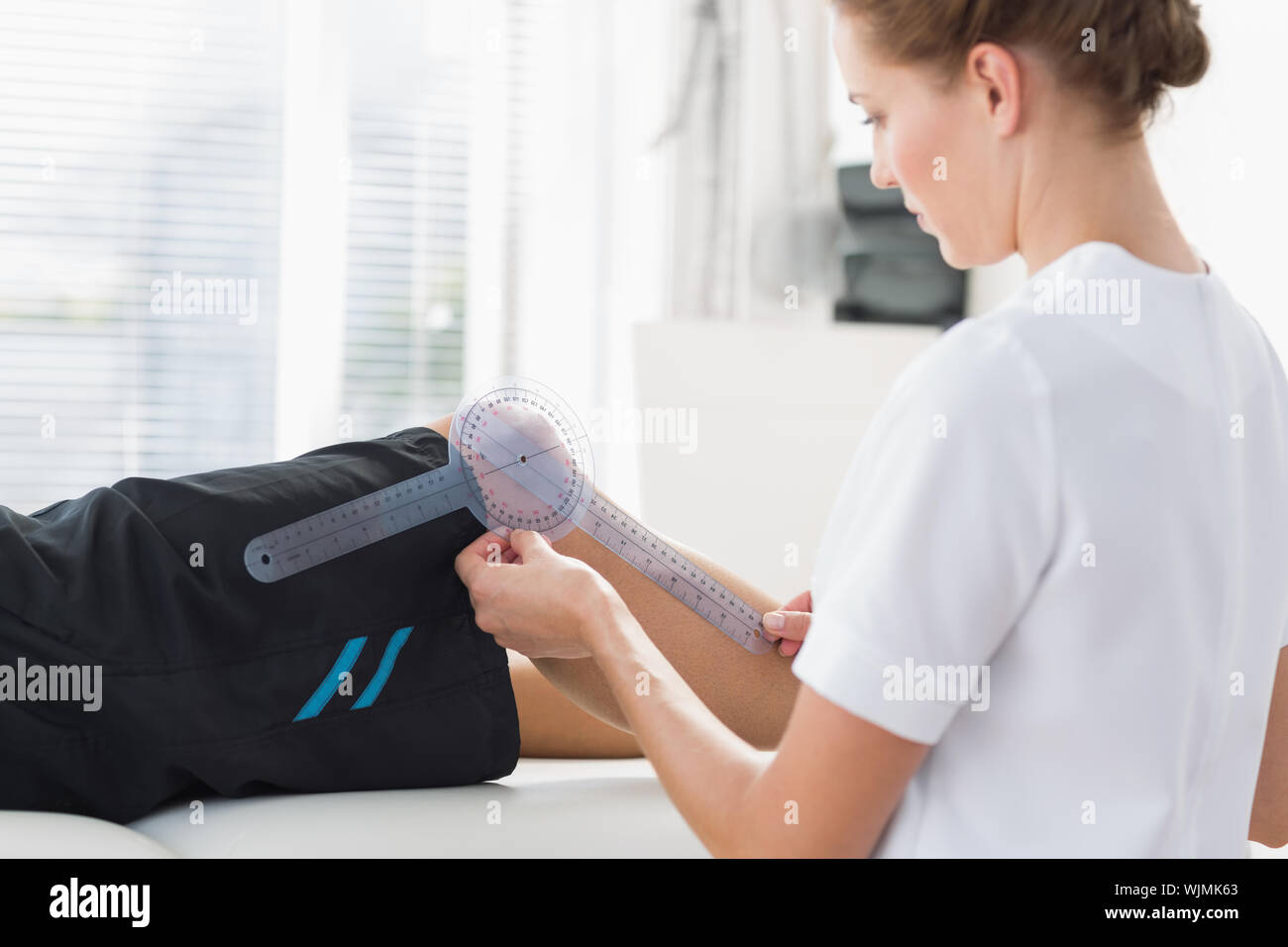 Female physiotherapist examining knee angle of man with goniometer ...