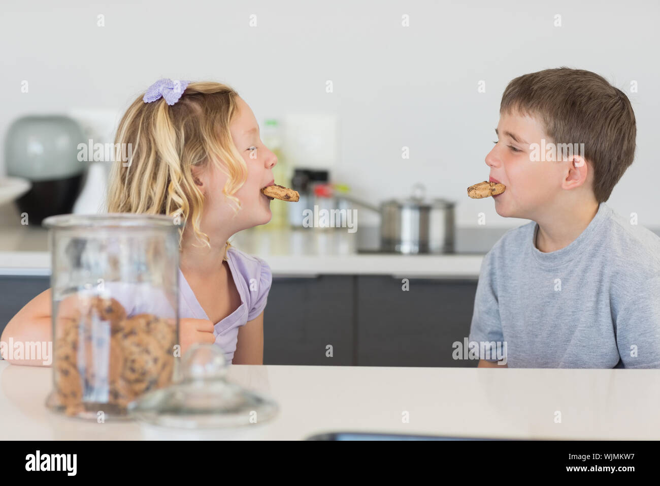 Happy playful siblings with cookies in mouth at kitchen counter Stock ...