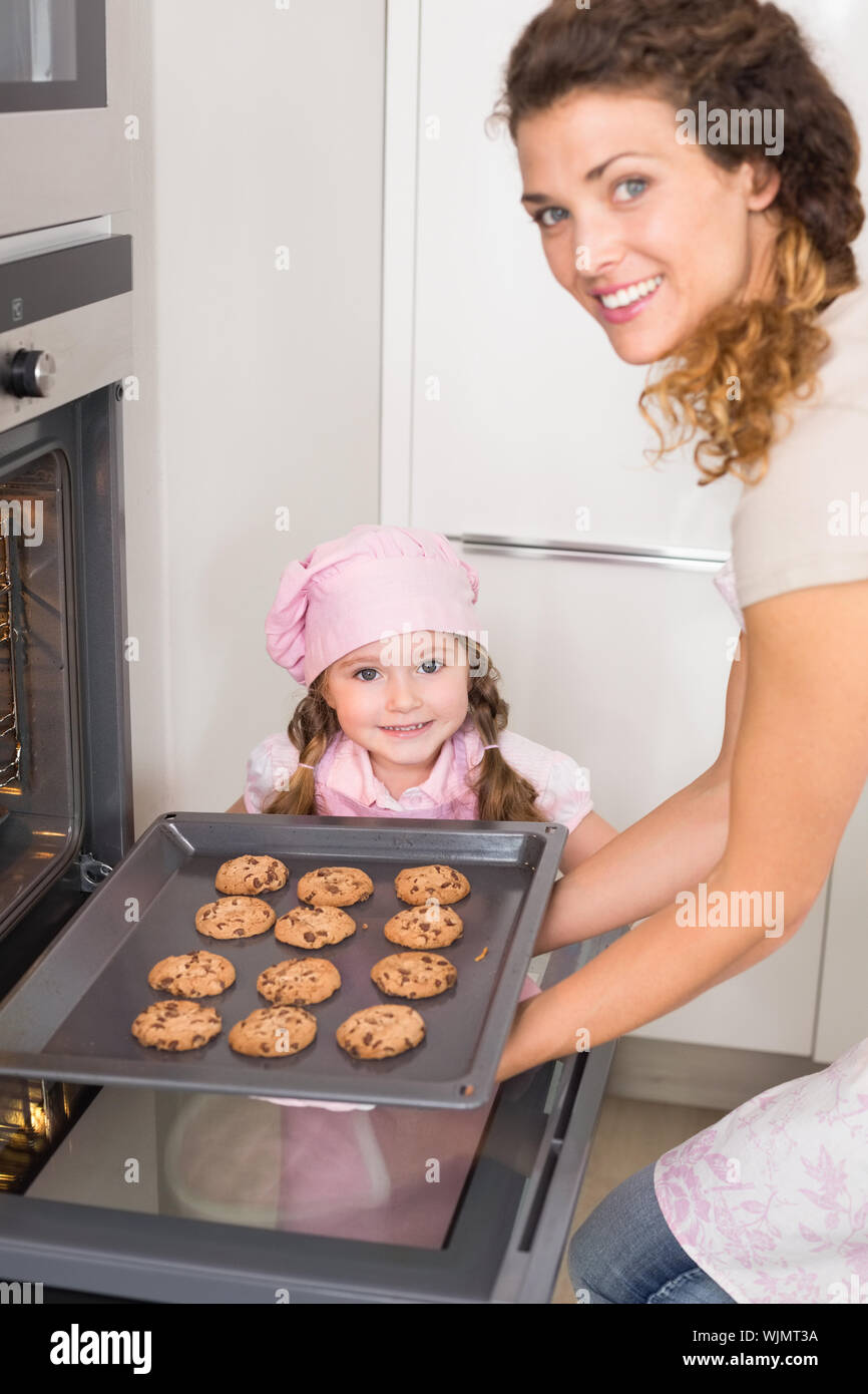 Mother taking cookies out of the oven with daughter at home in kitchen ...