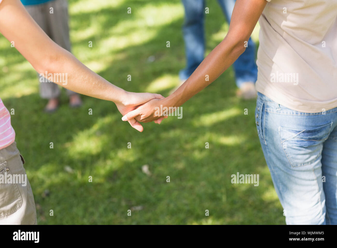 Close-up mid section of group of friends holding hands in the park ...