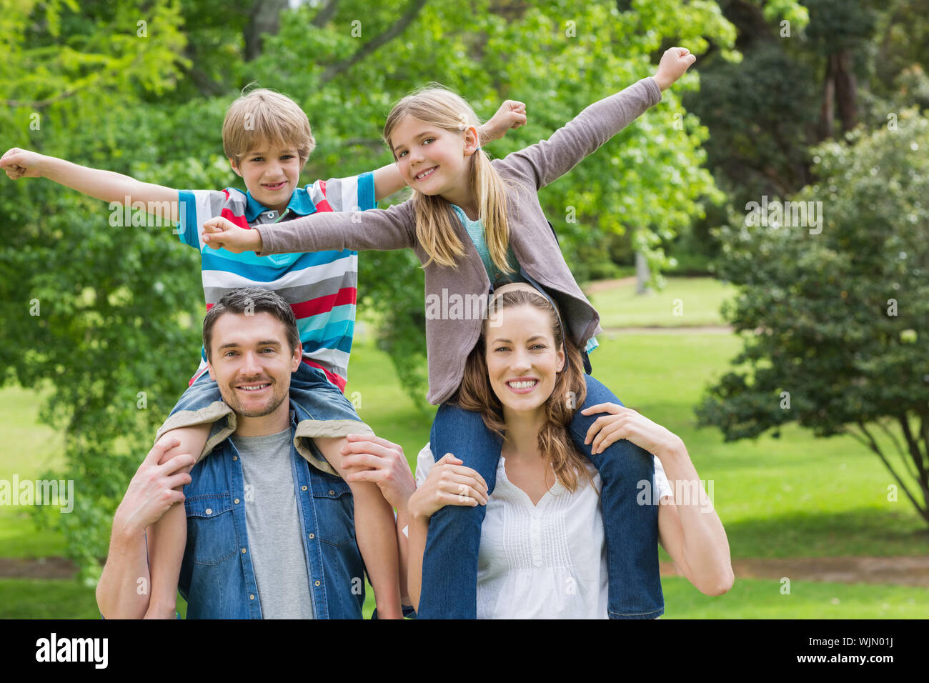 Portrait of happy parents carrying kids on shoulders at the park Stock ...