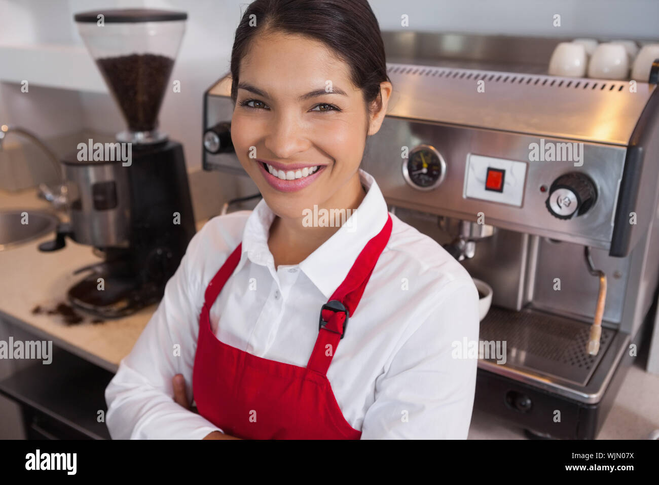 Happy young barista leaning against counter smiling at camera in a cafe ...