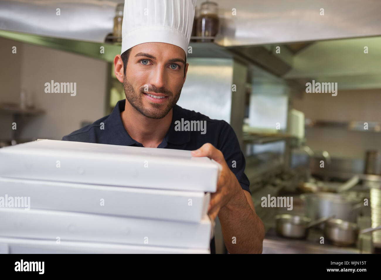 Happy pizza chef holding stack of pizza boxes in a commercial kitchen ...