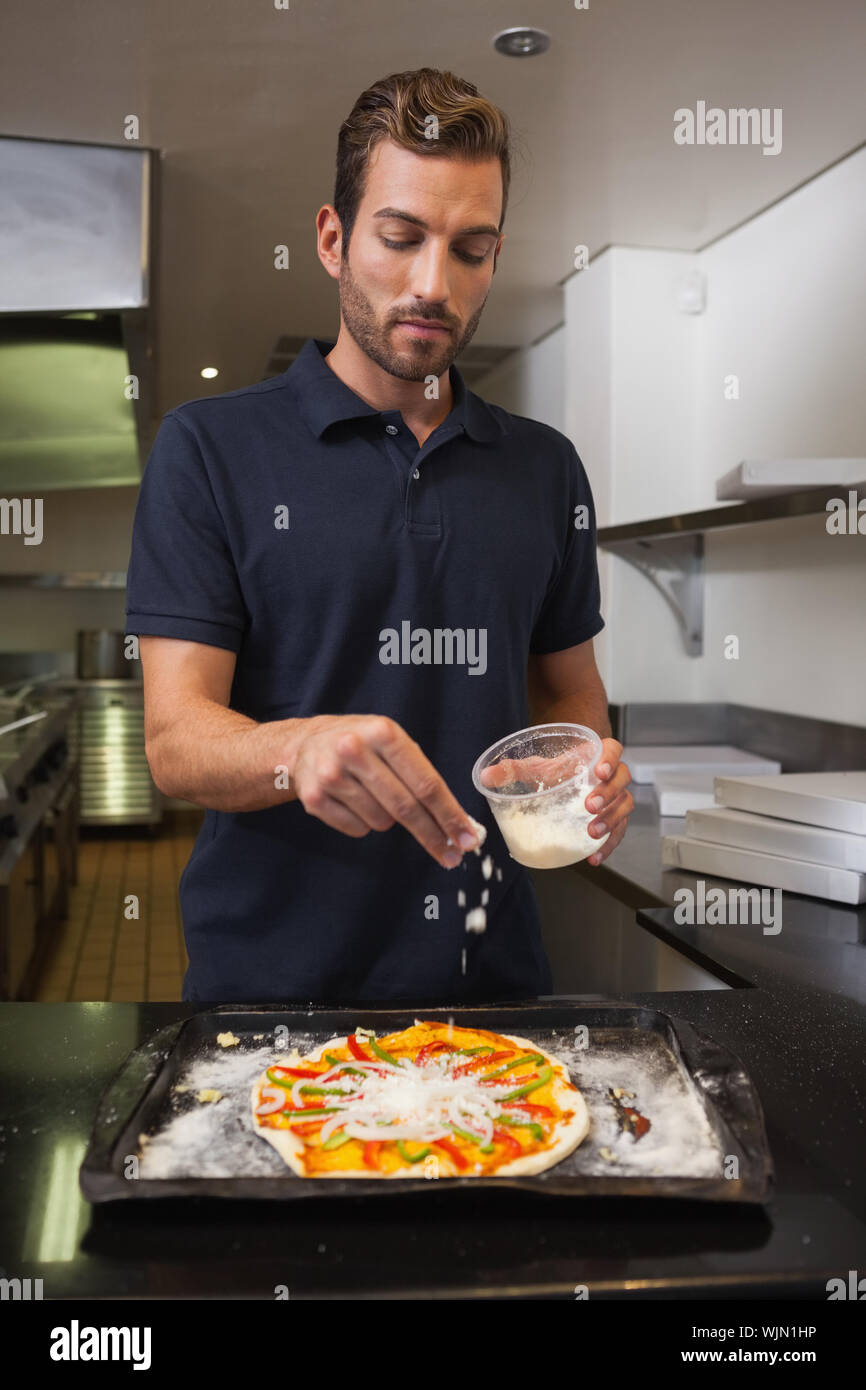 Pizza chef sprinkling cheese over pizza in a commercial kitchen Stock ...