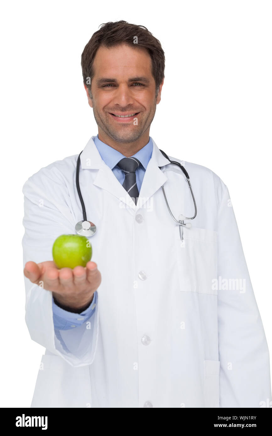 Happy doctor smiling and holding apple to camera on white background ...