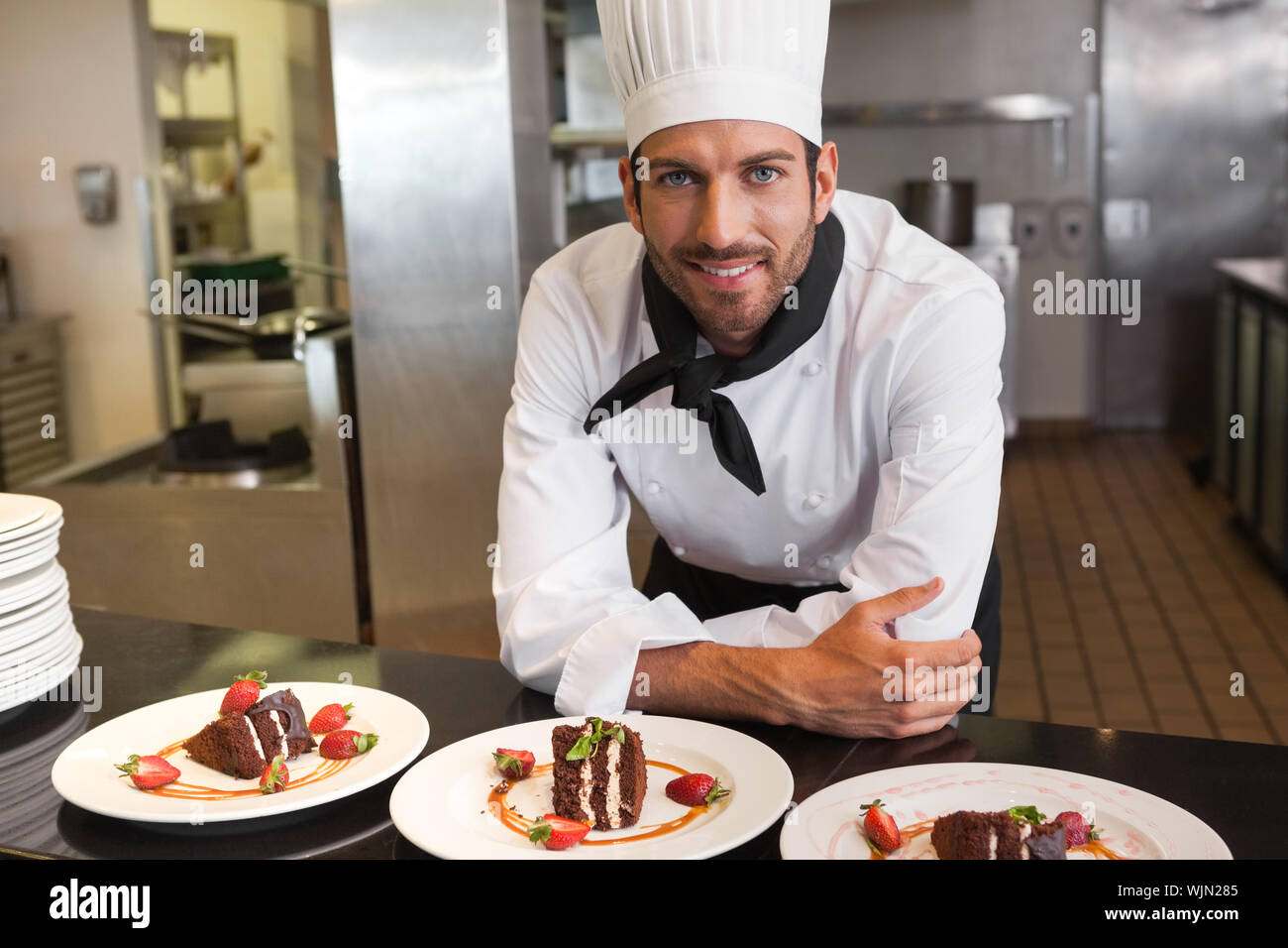 Happy chef looking at camera behind counter of desserts in a commercial ...