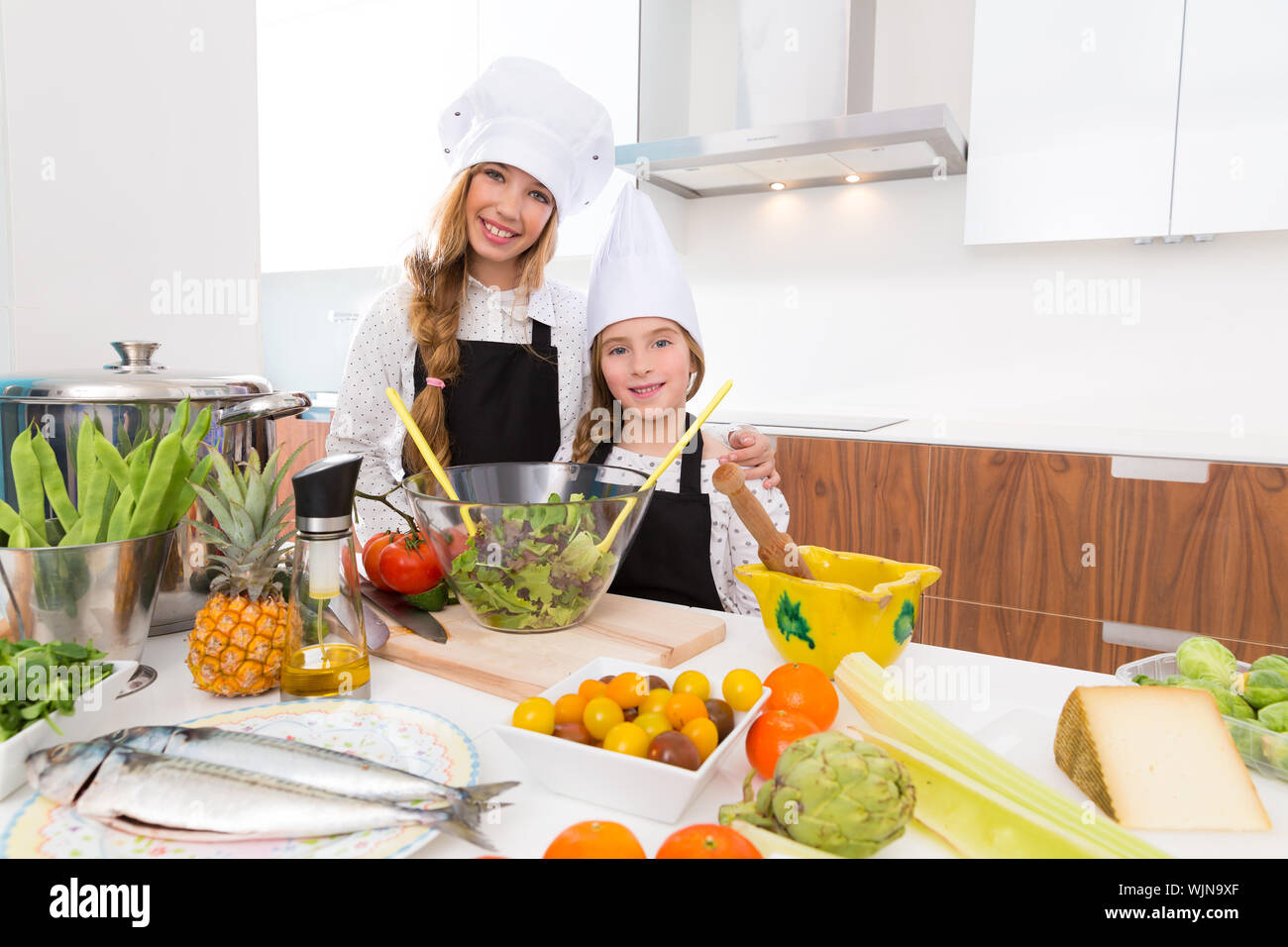 Kid girls junior chef friends hug together in countertop with food at ...