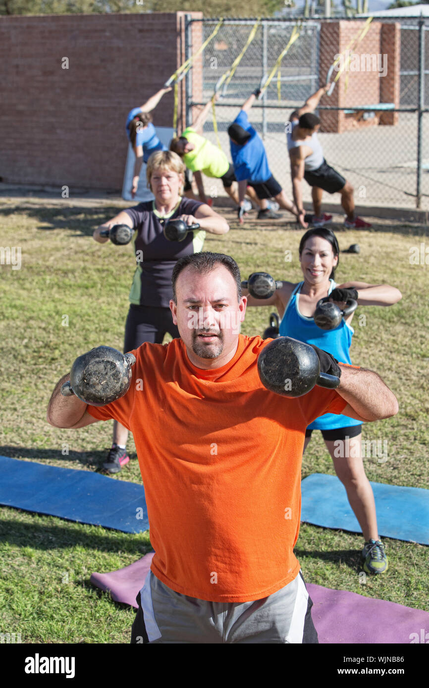 Confident man and group lifting weights in boot camp fitness class ...