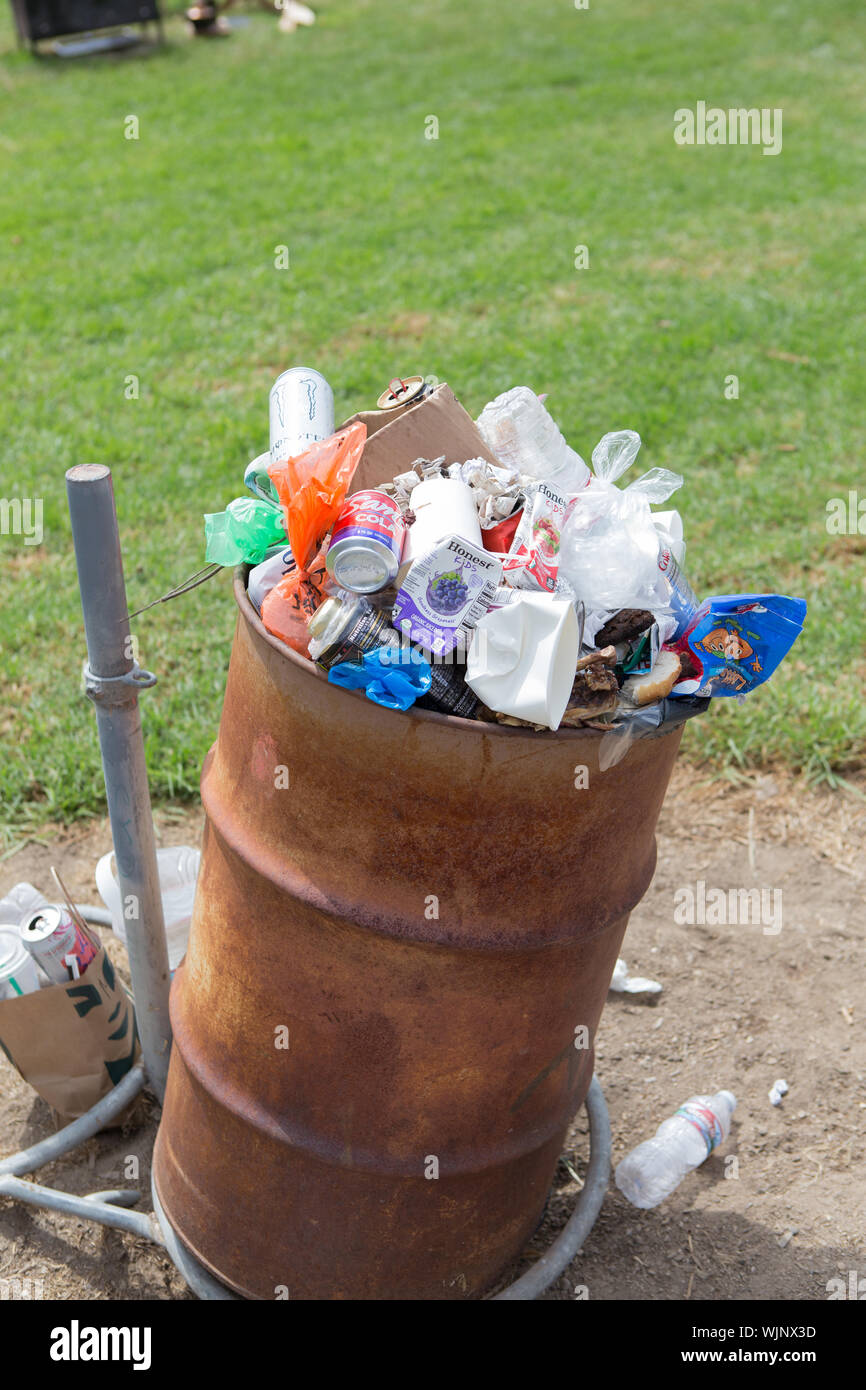 Old rusty trash can overflowing with plastic bottles, food and drink ...