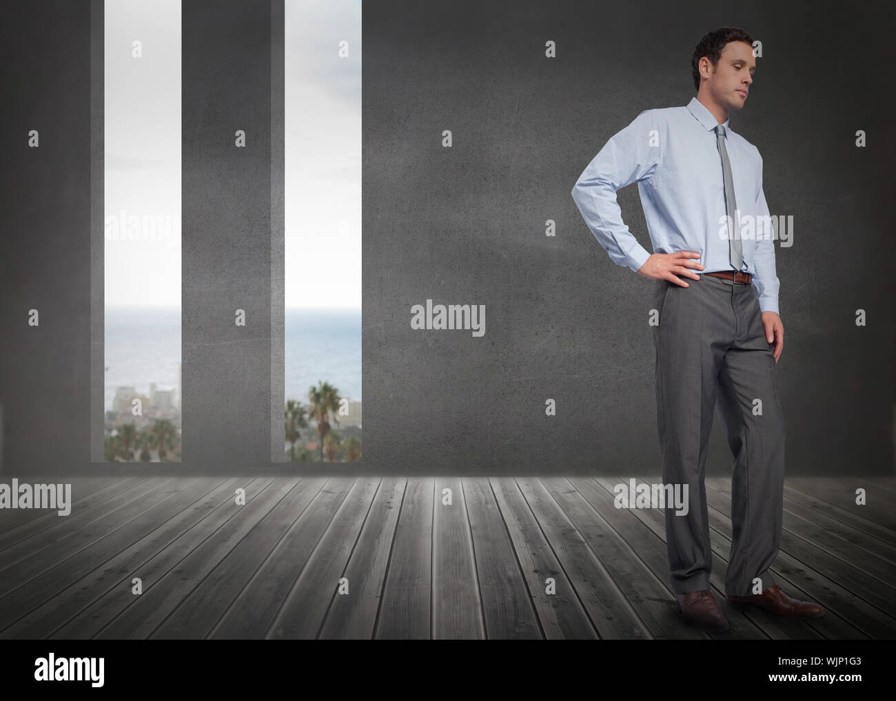 Serious businessman with hand on hip against grey room with windows ...