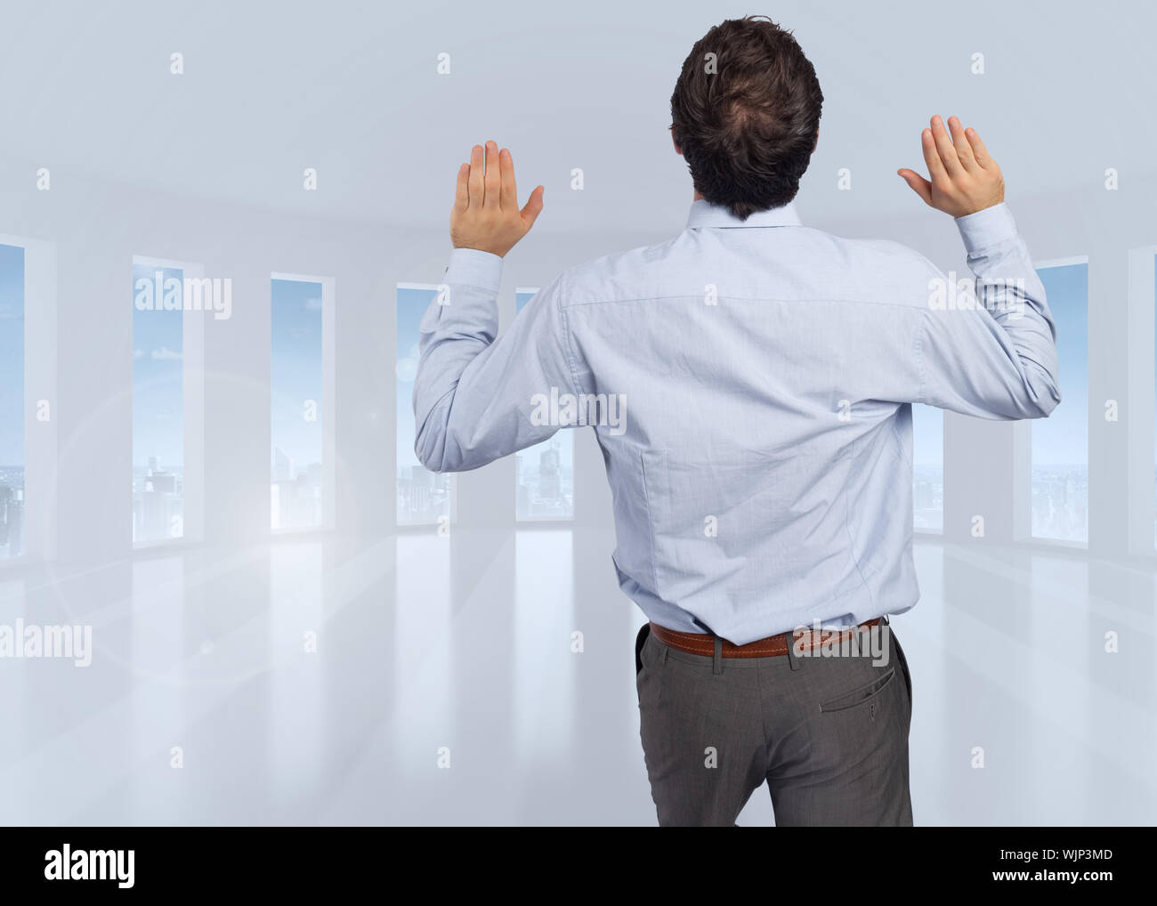 Businessman standing with hands up against bright white room with ...