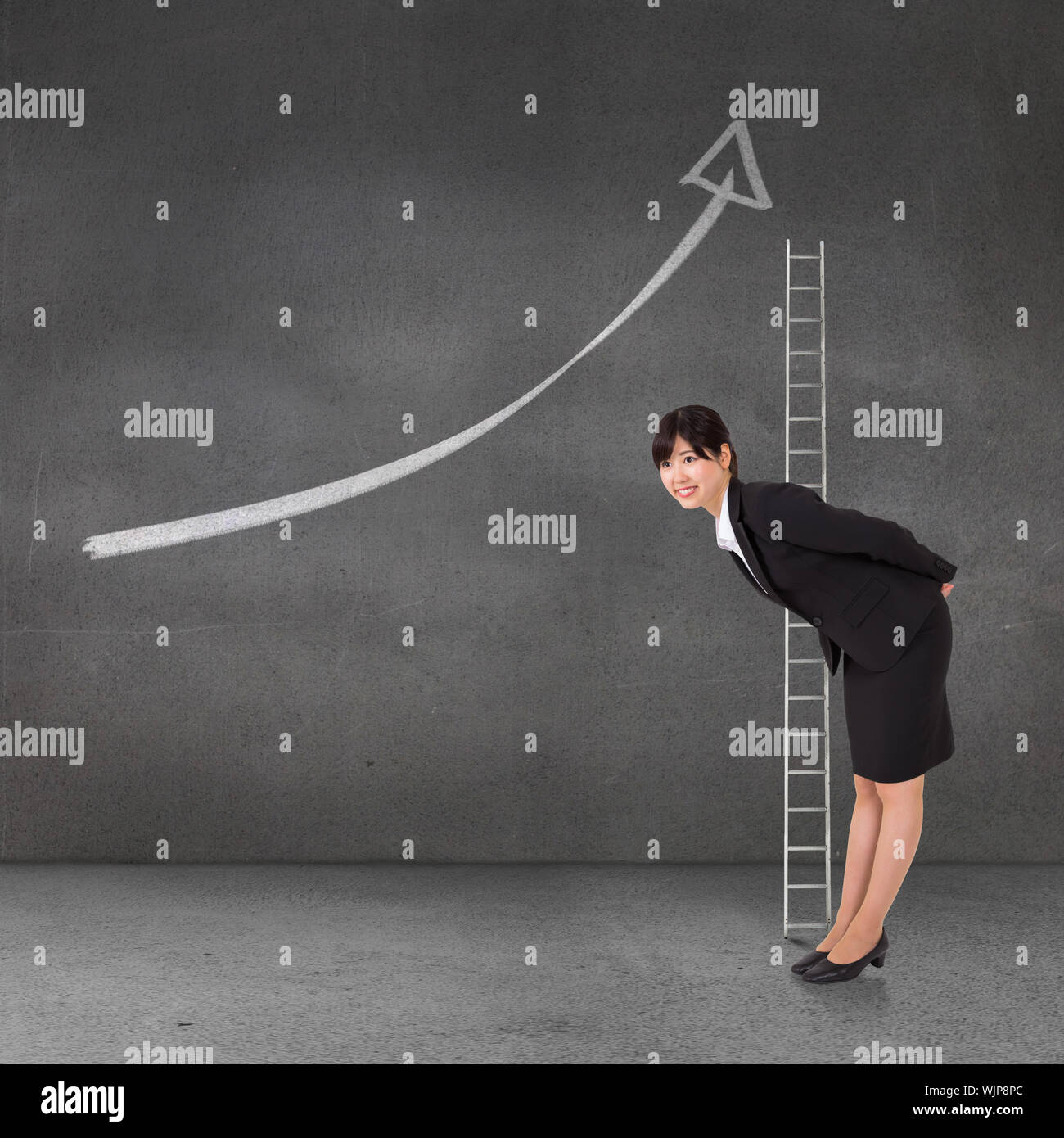 Smiling businesswoman bending against arrow and ladder in grey room ...