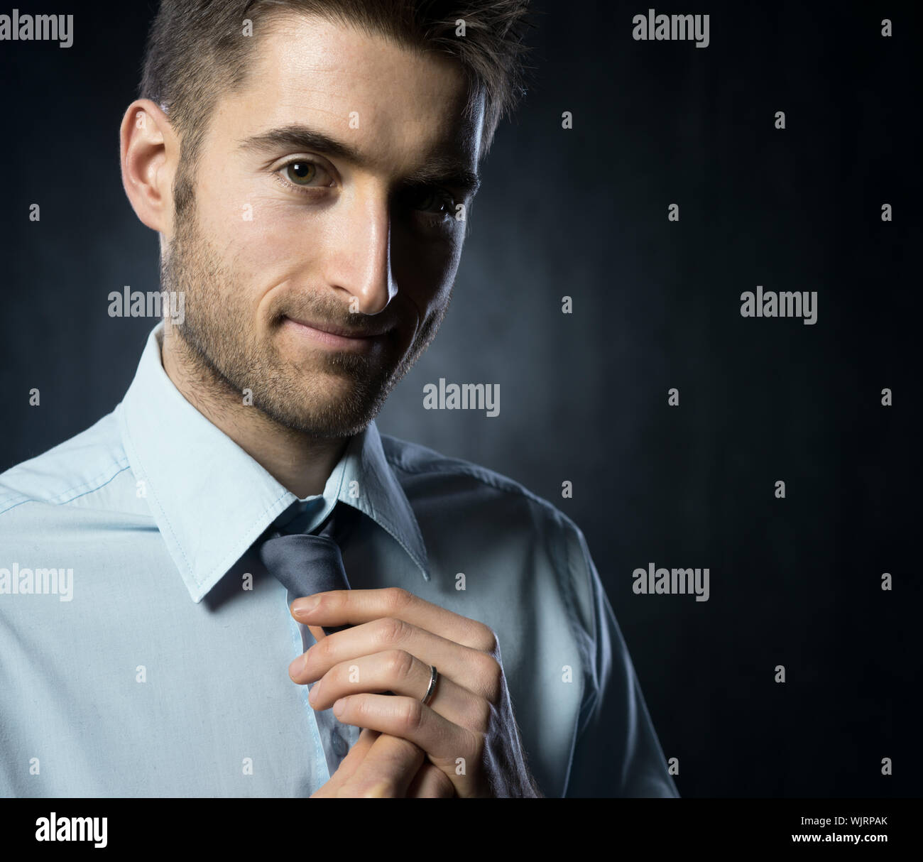 Young elegant man adjusting tie knot and smiling Stock Photo - Alamy