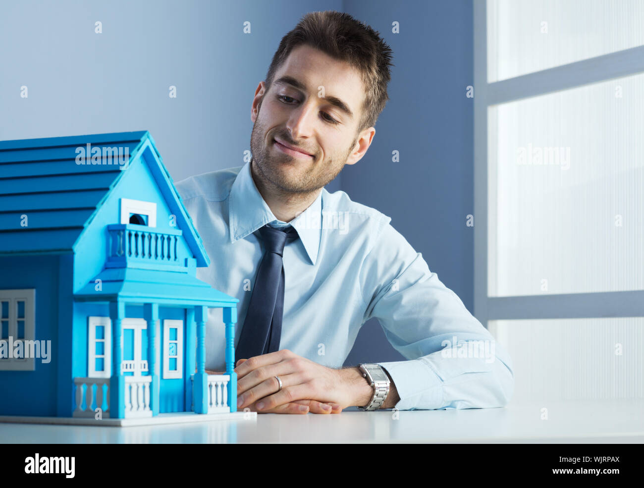 Friendly real estate agent with light blue model house Stock Photo - Alamy