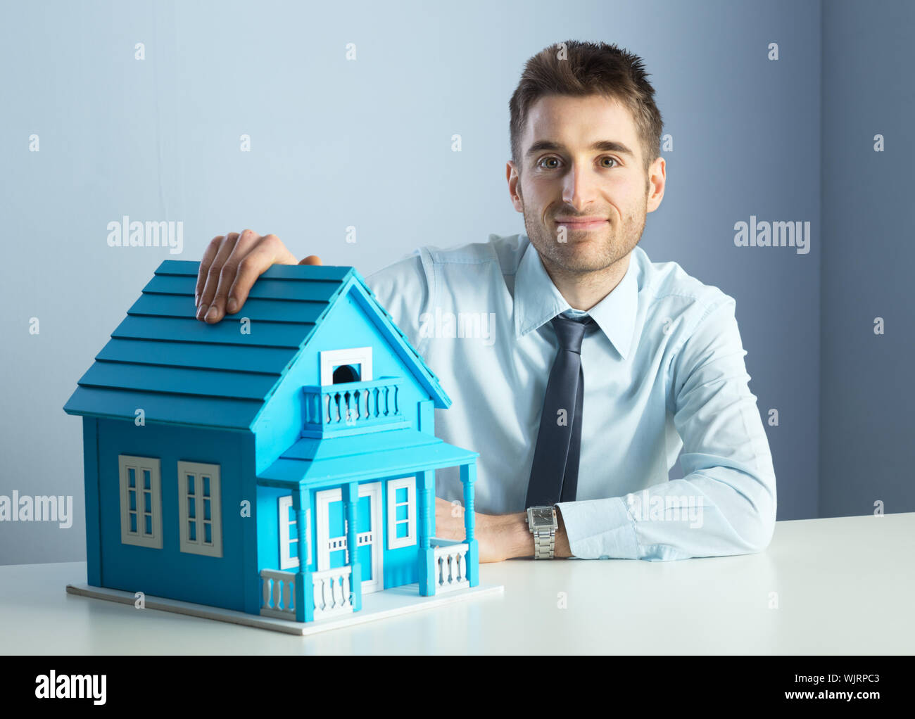 Friendly real estate agent with light blue model house Stock Photo - Alamy