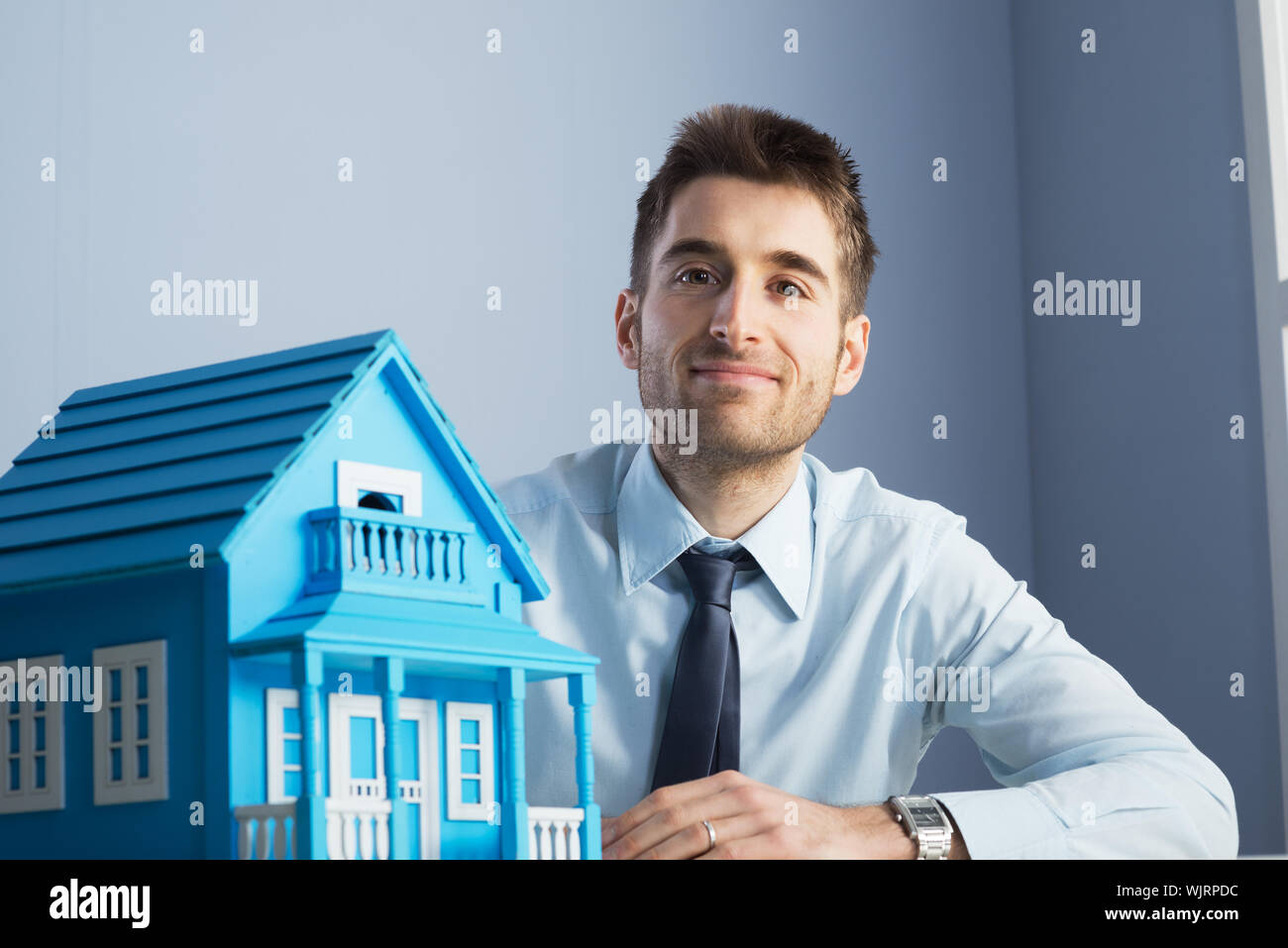Friendly real estate agent with light blue model house Stock Photo - Alamy