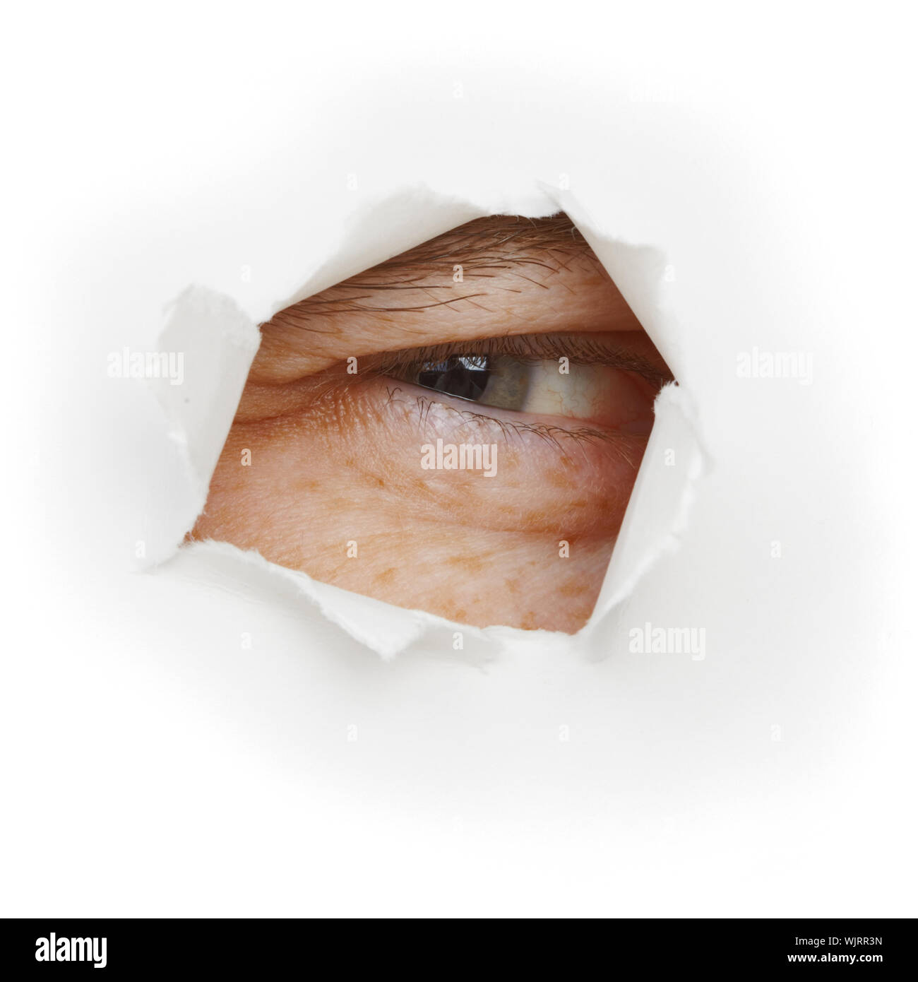 Squinting eye looks through a hole in white paper Stock Photo - Alamy