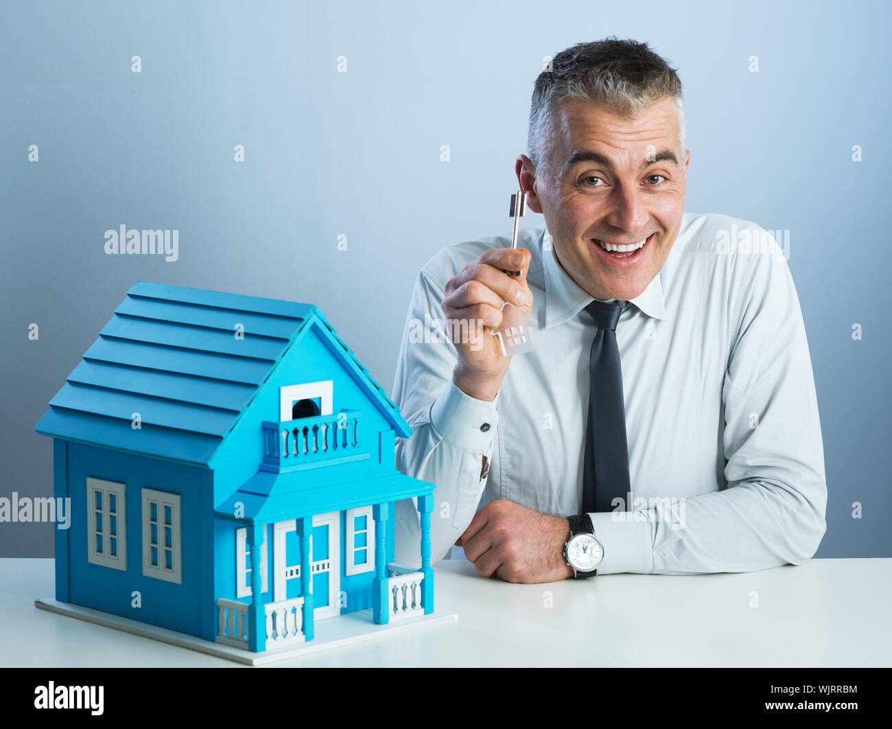 Real estate agent at desk with light blue model house Stock Photo - Alamy