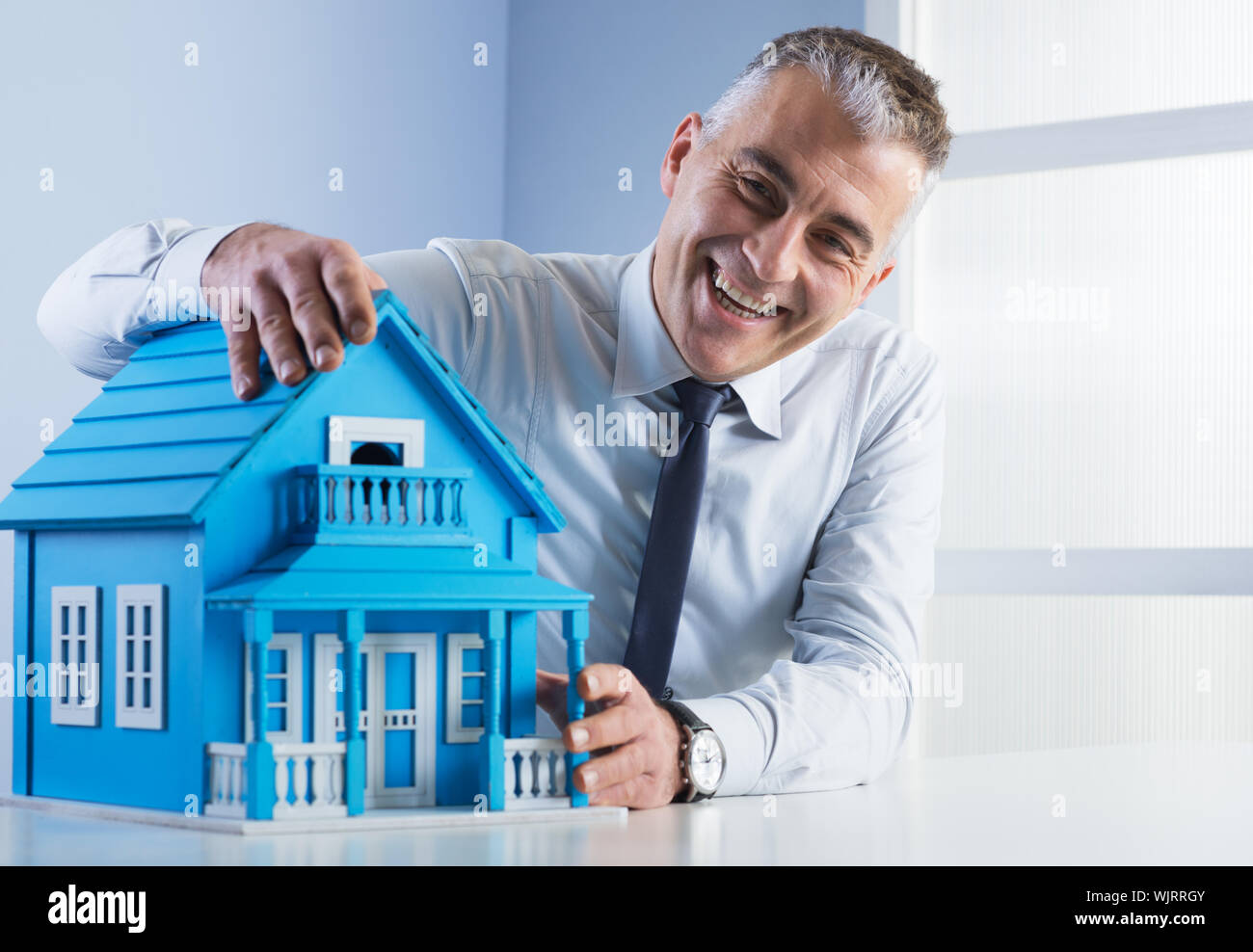 Real estate agent at desk with light blue model house Stock Photo - Alamy