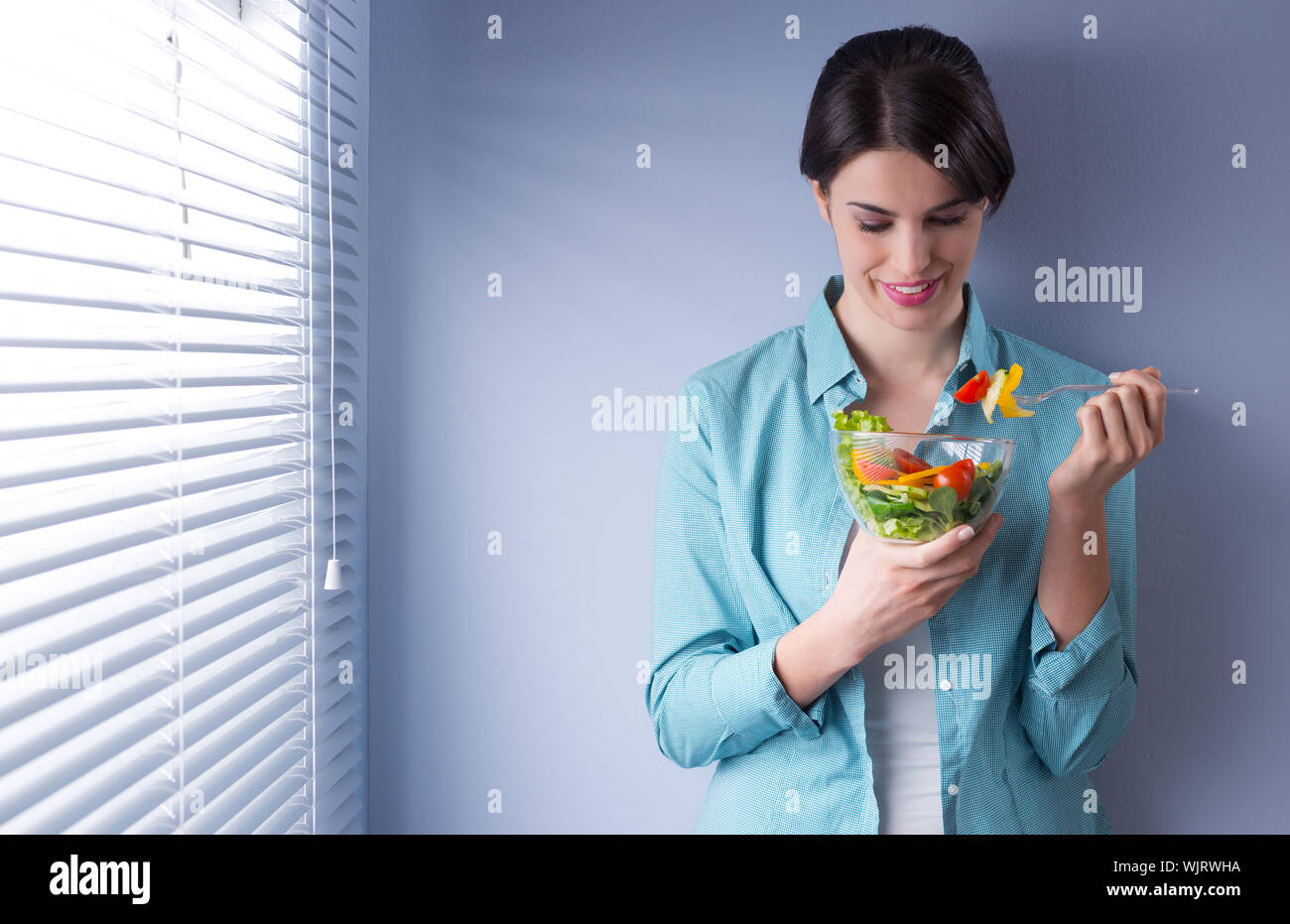 Woman smiling and eating salad in front of a window Stock Photo - Alamy