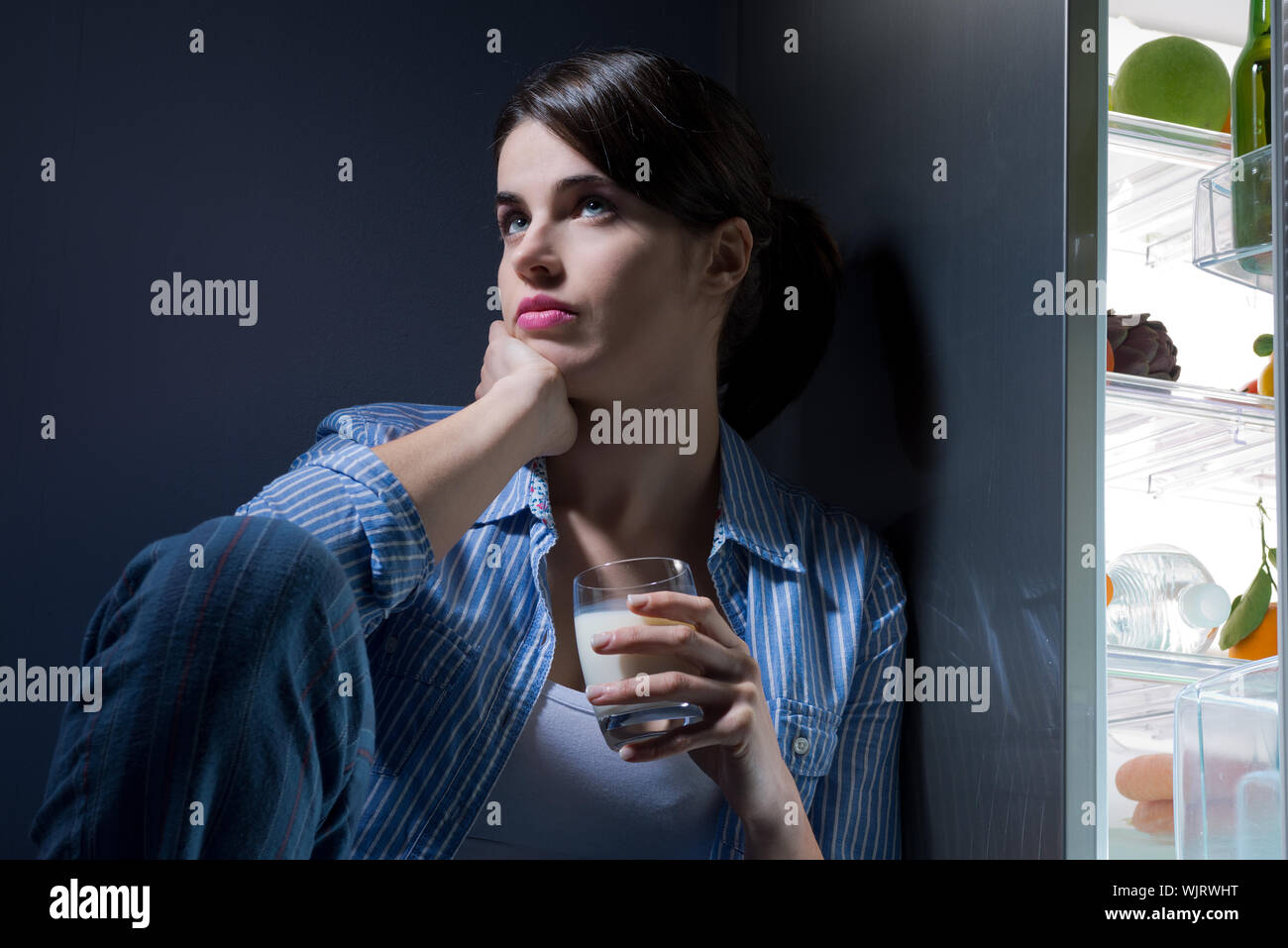 Sleepless sad woman sitting on kitchen floor having a glass of milk ...