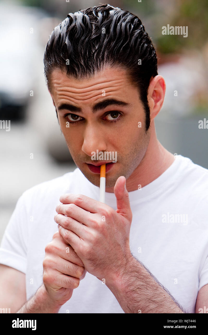 Handsome Caucasian man wearing white shirt lighting a filter cigarette ...