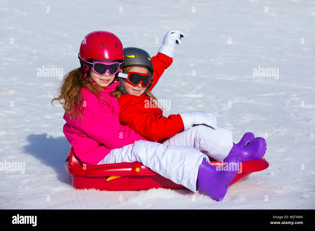 Kid girls playing sled in winter snow with helmets and goggles Stock ...