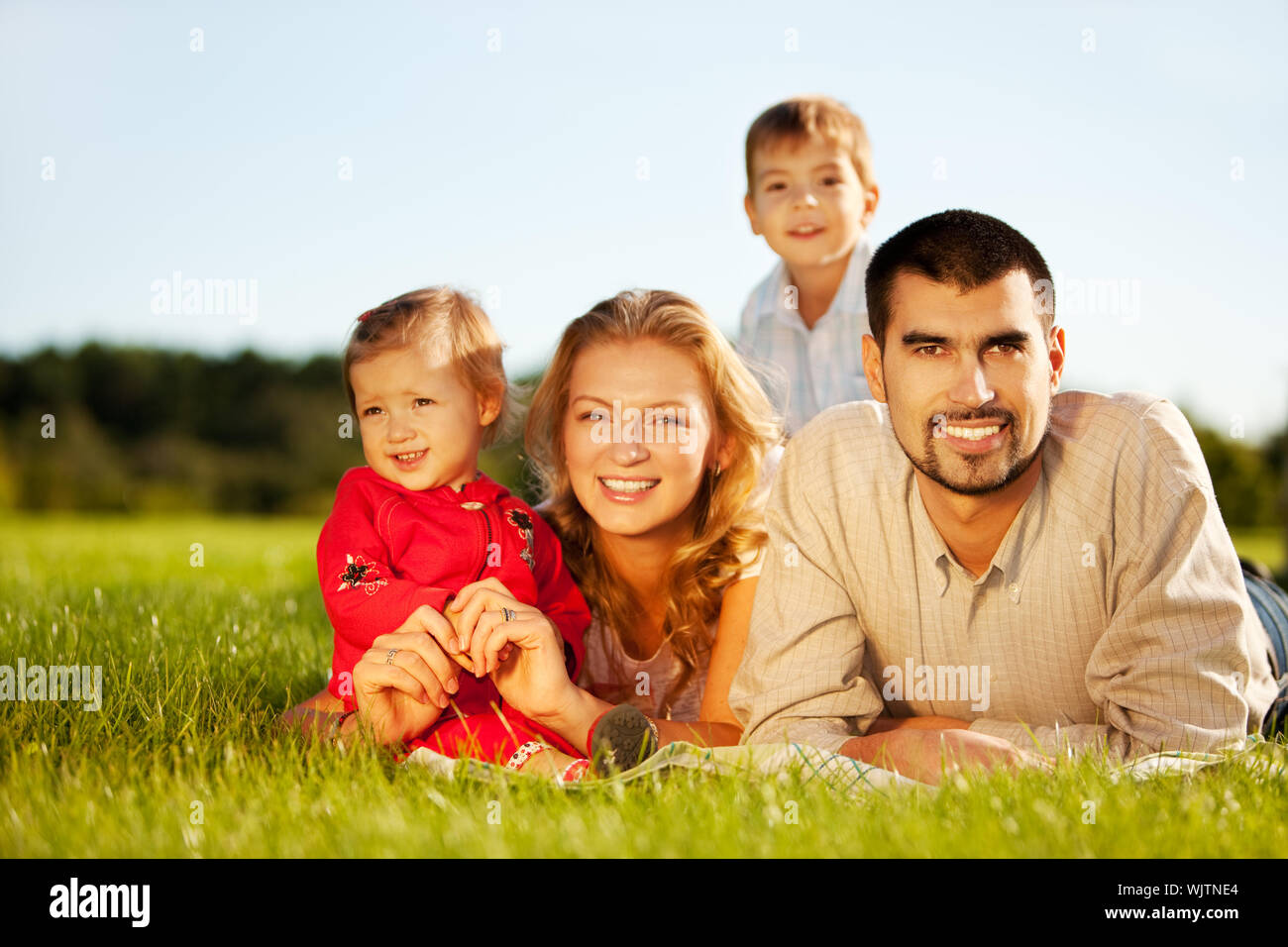 Happy family of 4 people lying ona grass under summer sun. Focus is on ...