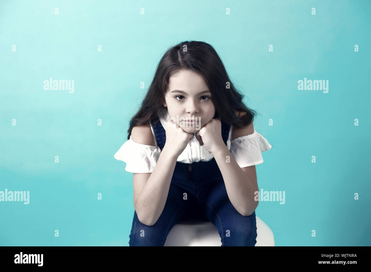 Girl prop chin on hands on blue background. Child with long brunette ...