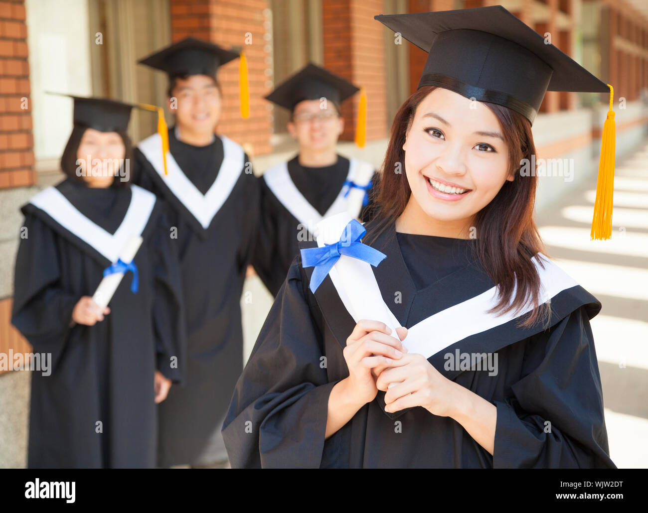 smiling college graduate holding diploma with classmates Stock Photo ...