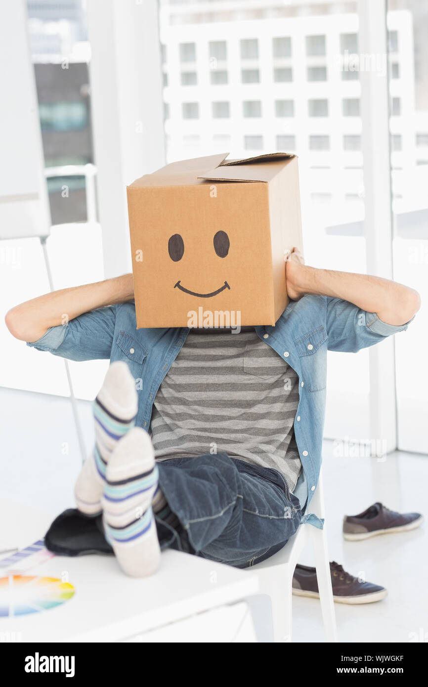 Casual young man with happy smiley box over face while sitting on chair ...