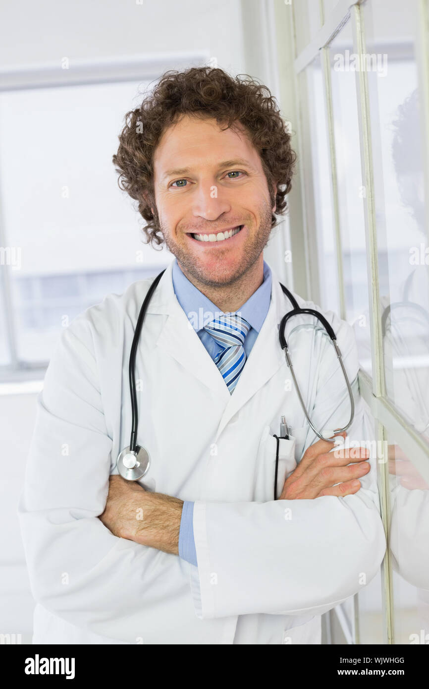 Portrait of a happy handsome male doctor standing with arms crossed in ...