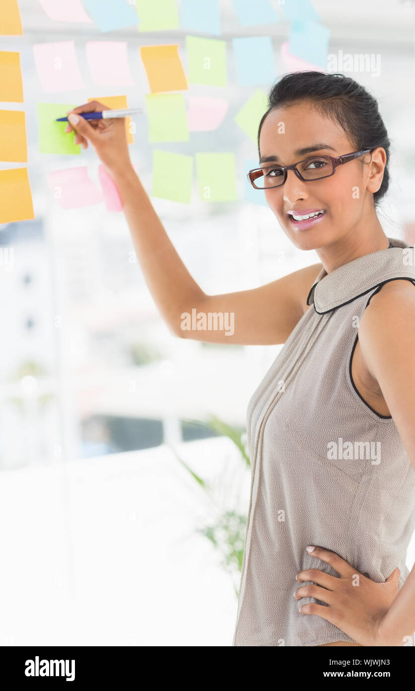 Designer writing on sticky notes on window smiling at camera in ...