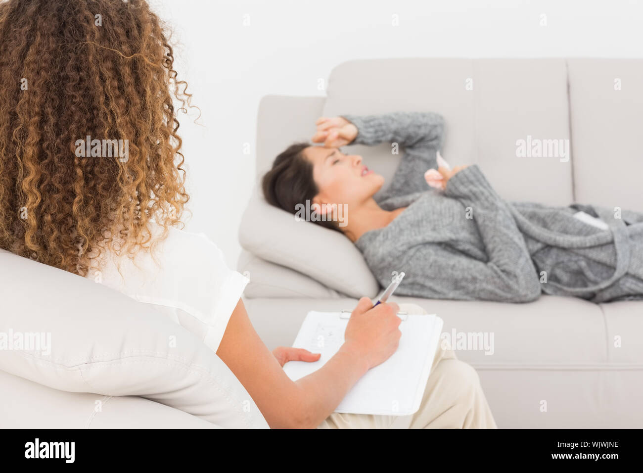 Therapist taking notes on her crying patient on the sofa at therapy ...