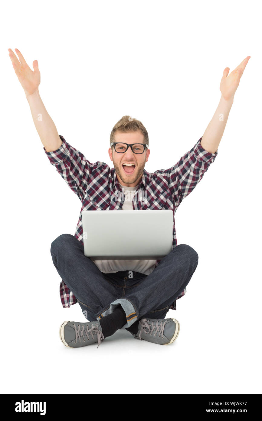Handsome man cheering at camera with laptop sitting on floor on white ...