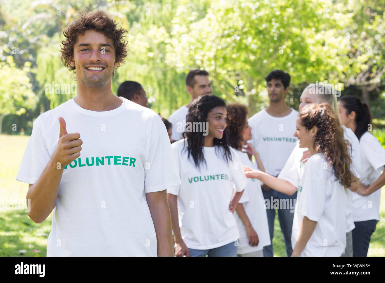 Confident male volunteer showing thumbs up with friends disucssing in ...