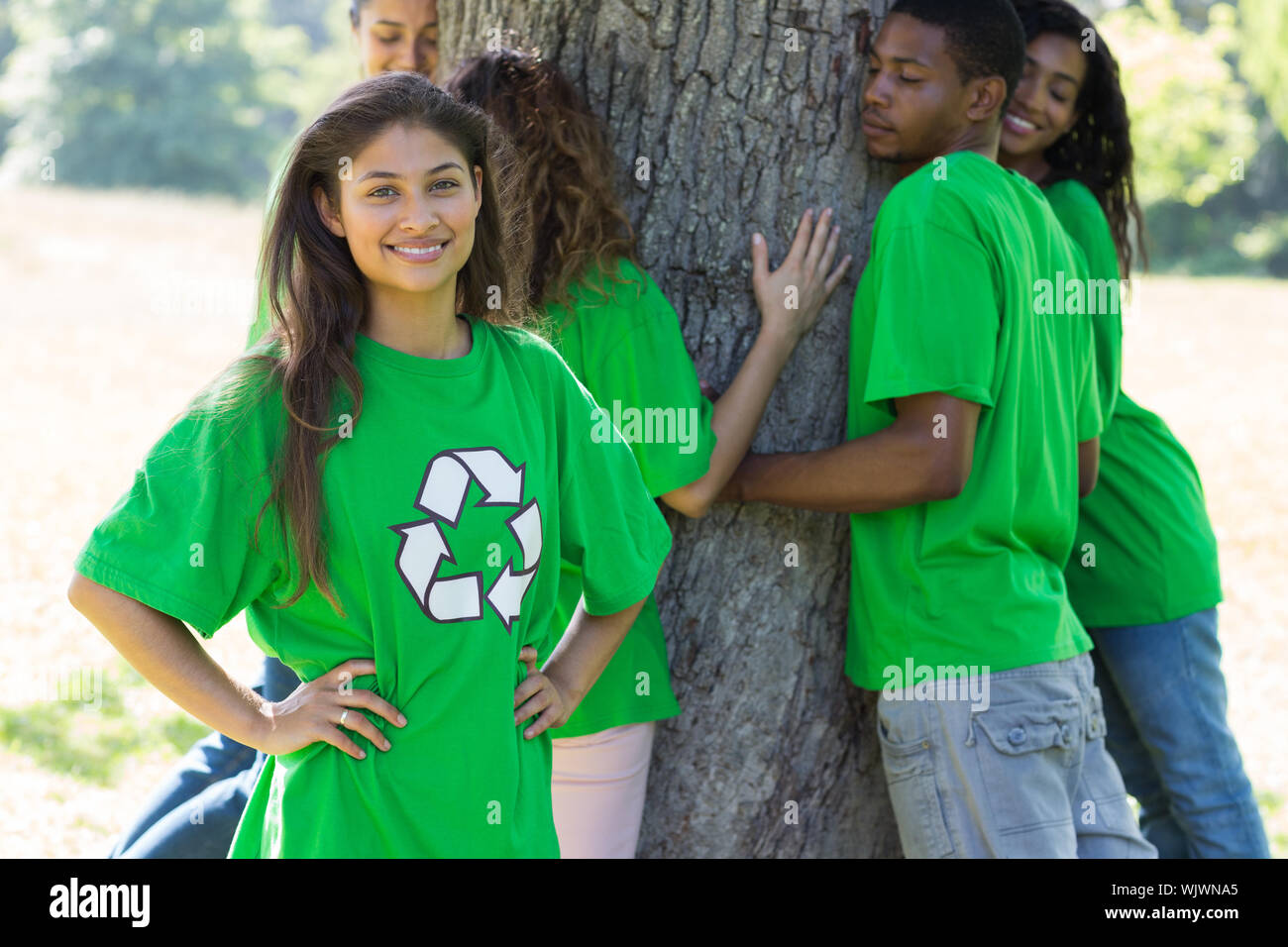 Portrait of female environmentalist at park with friends hugging tree ...