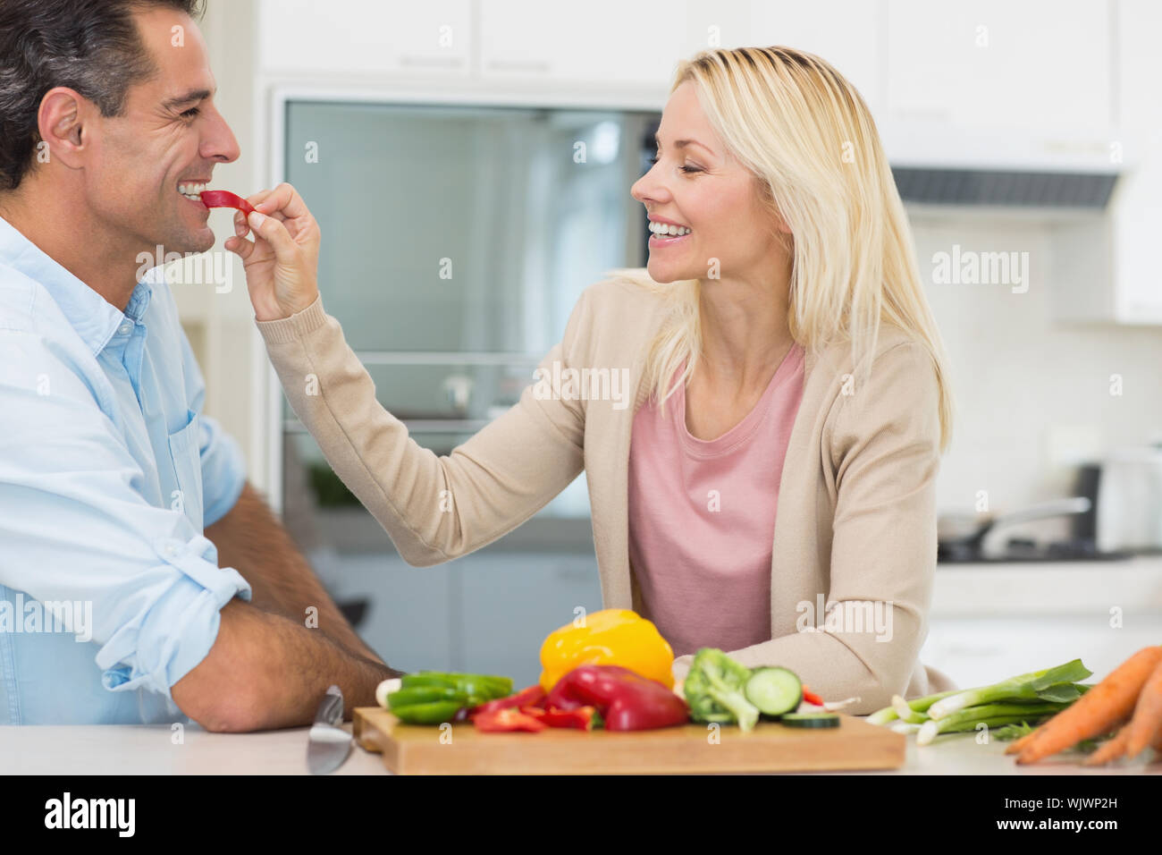 Happy loving woman feeding man vegetable in the kitchen at home Stock ...