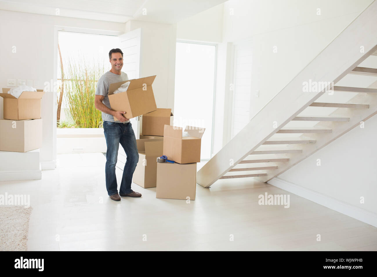 Portrait of a smiling man carrying boxes in a new house Stock Photo - Alamy