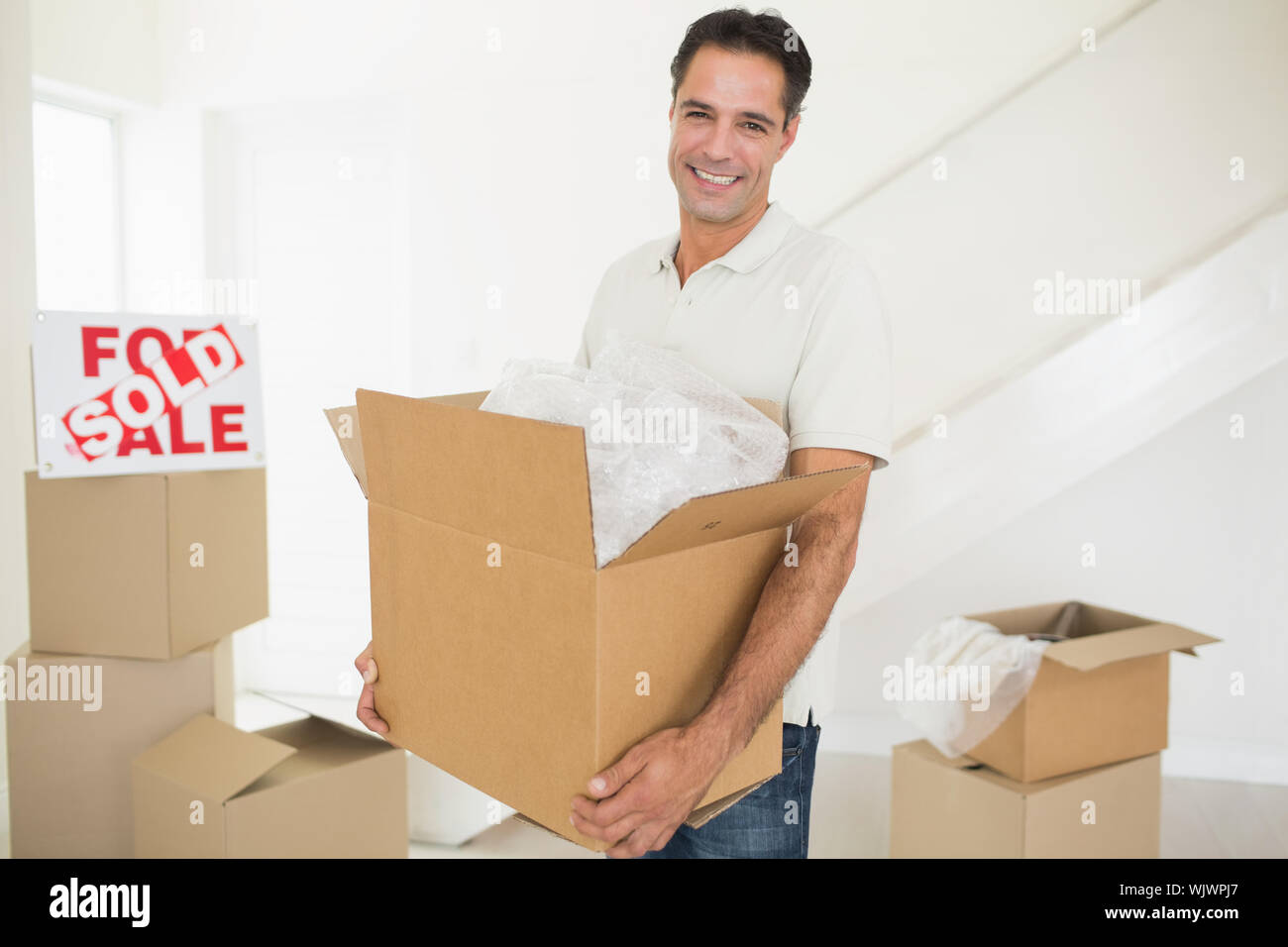 Portrait of a smiling man carrying boxes in a new house Stock Photo - Alamy