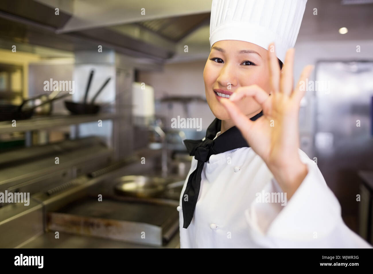 Portrait of a smiling female cook gesturing okay sign in the kitchen ...