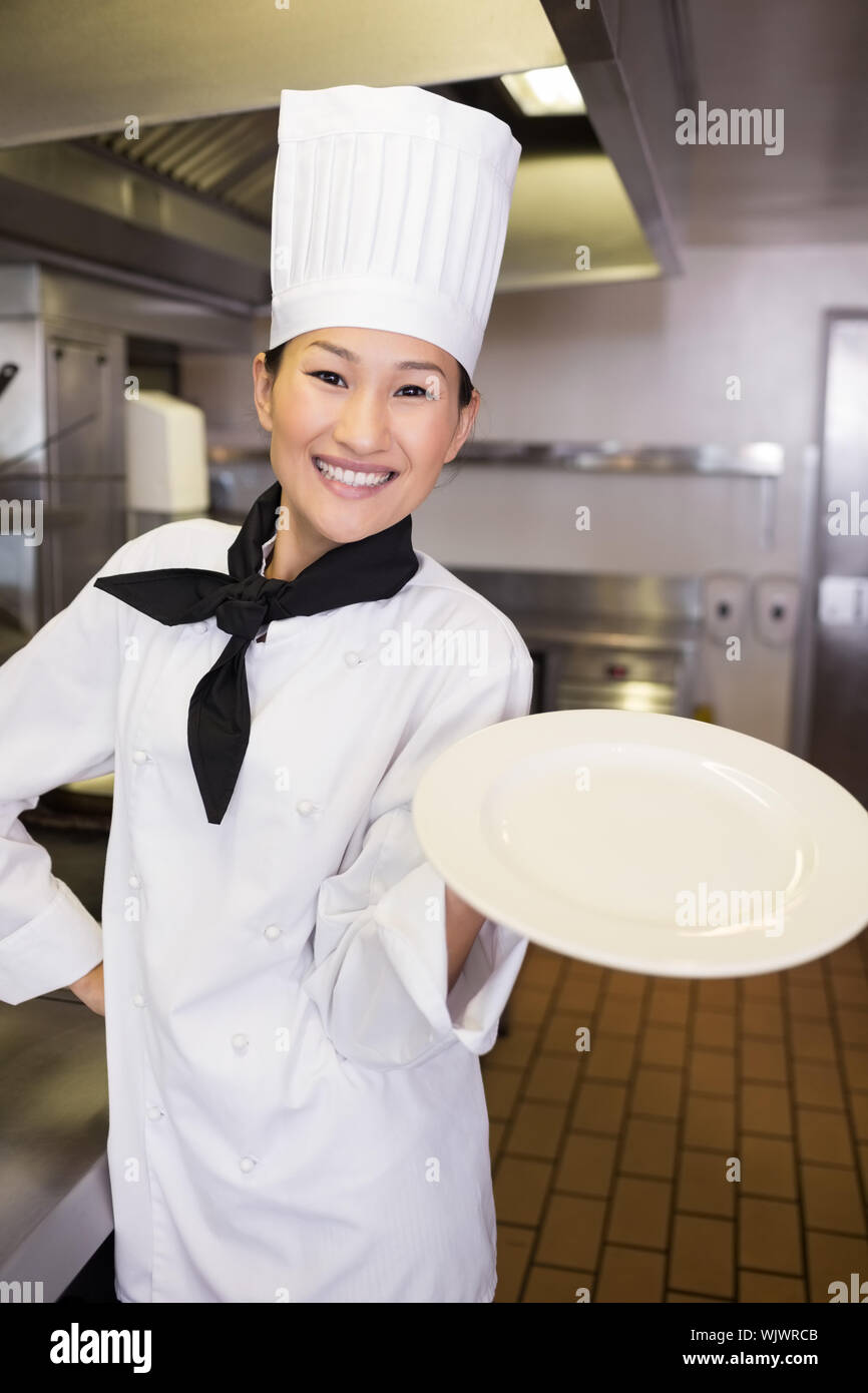 Portrait of a smiling female cook holding an empty plate in the kitchen ...
