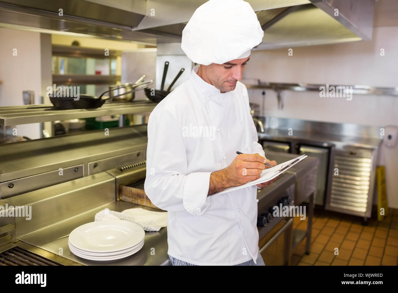 Side view of a concentrated male cook writing on clipboard in the ...
