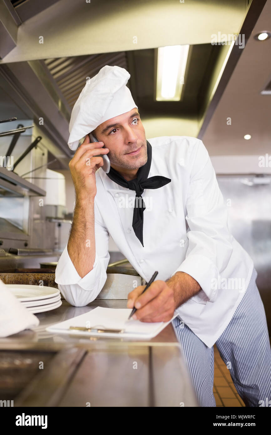 Concentrated male cook writing on clipboard while using cellphone in ...